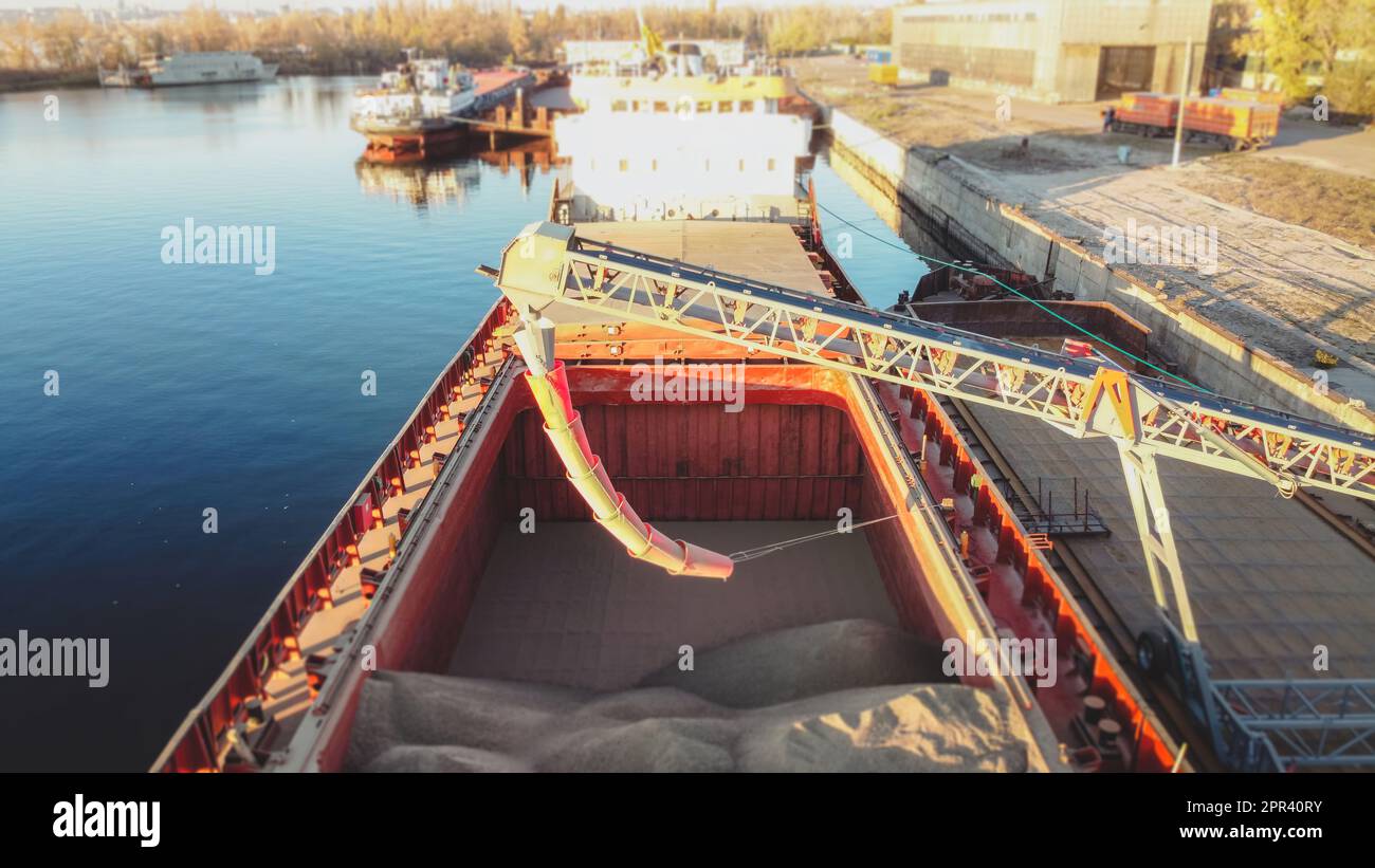 Grain loading in hold of bulk carrier ship with elevator crane closeup ...