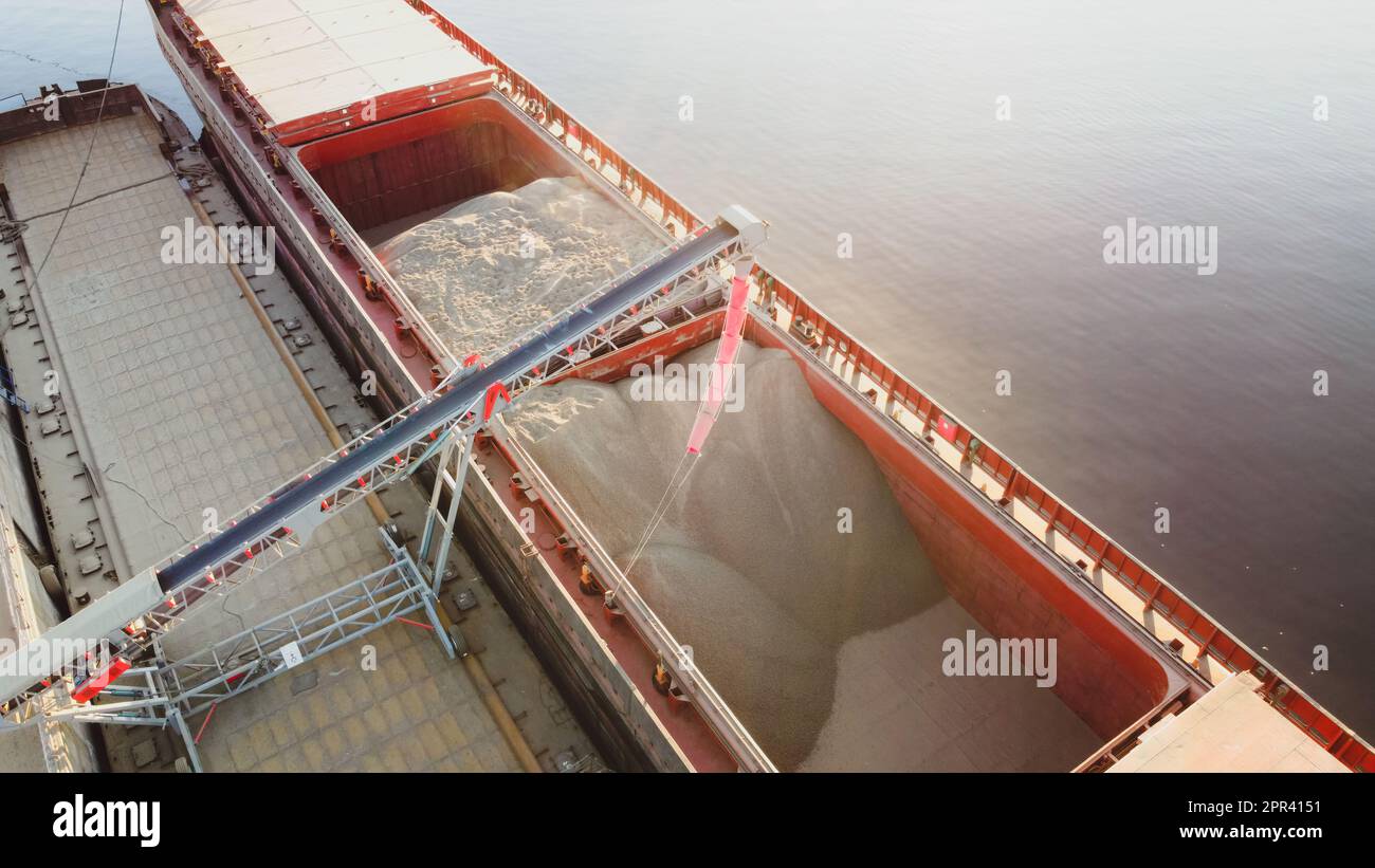 Grain loading in hold of bulk carrier ship with elevator crane closeup. Port grain elevator ...