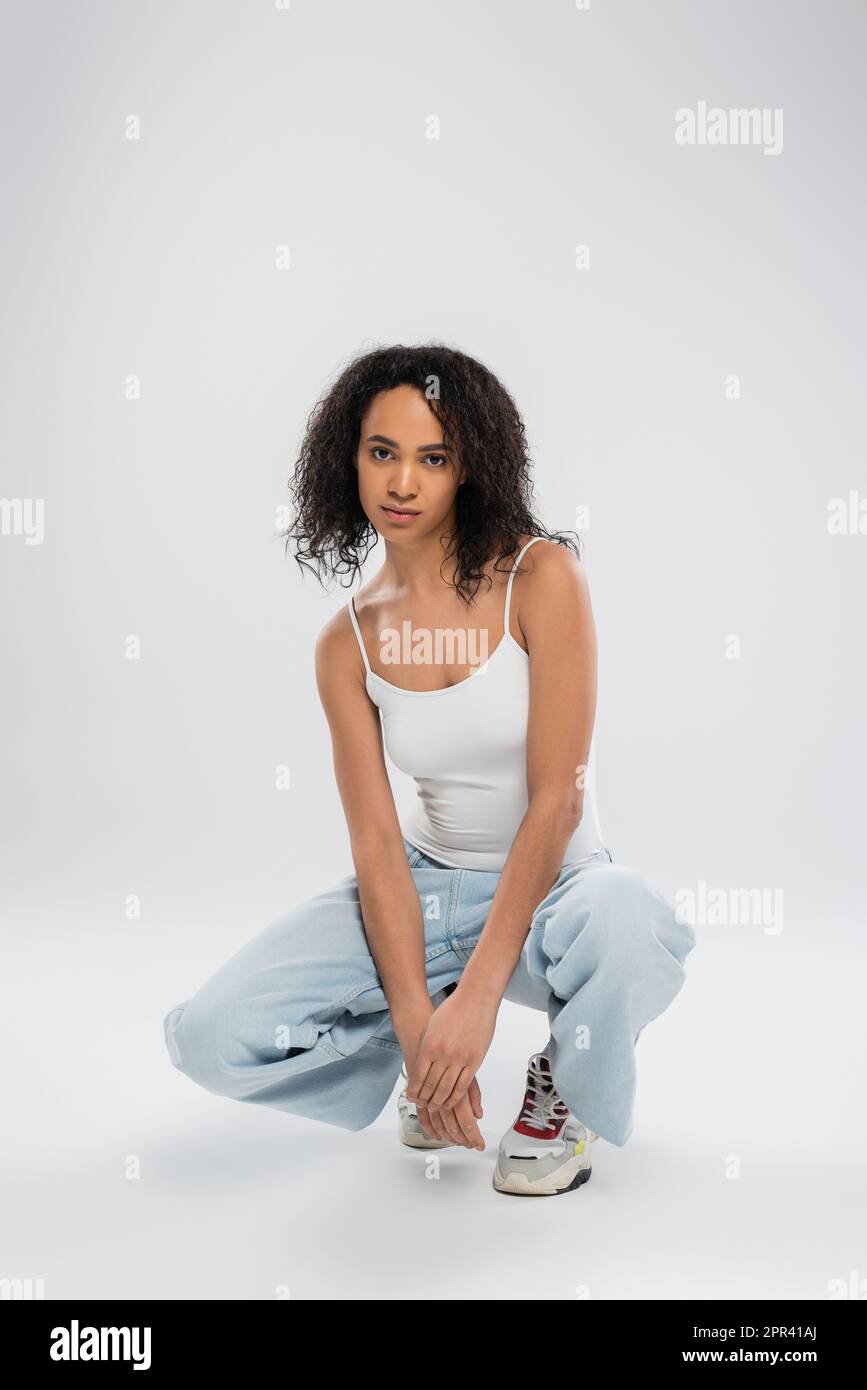 full length of african american woman in white tank top and jeans with ...