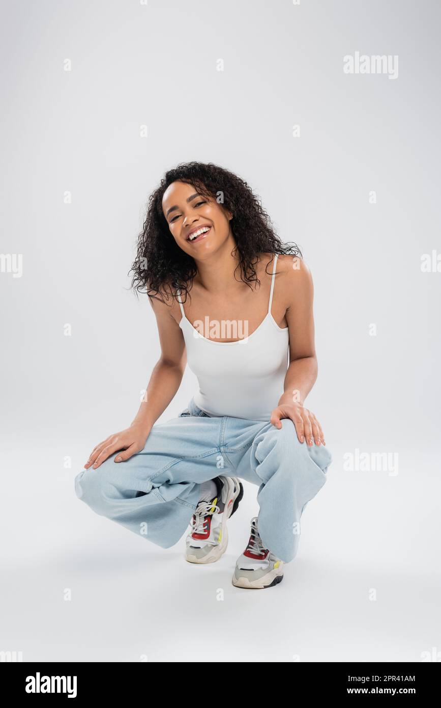full length of overjoyed african american woman in jeans and sneakers ...