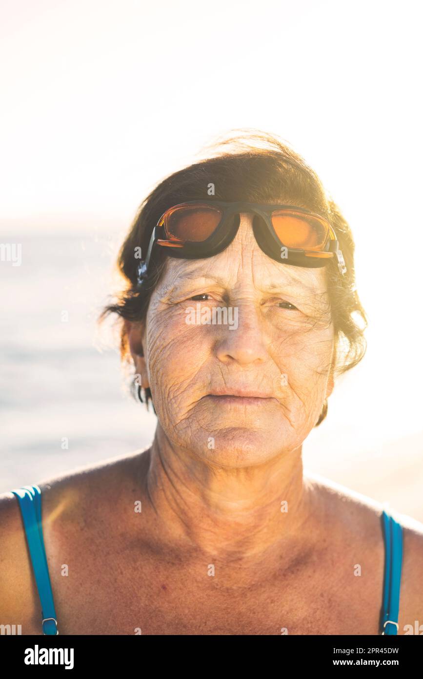 Senior woman at the beach, standing by the sea. Wearing a blue swimsuit ...