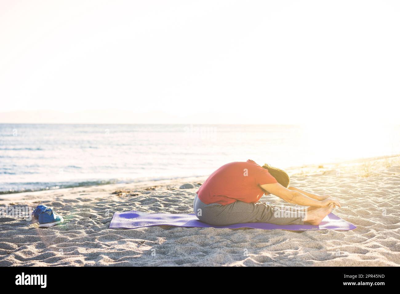 Senior woman at the beach, doing exercise on yoga mat, stretching her ...