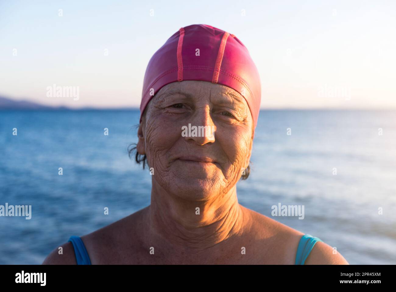 Senior woman at the beach, standing by the sea. Wearing a blue swimsuit ...