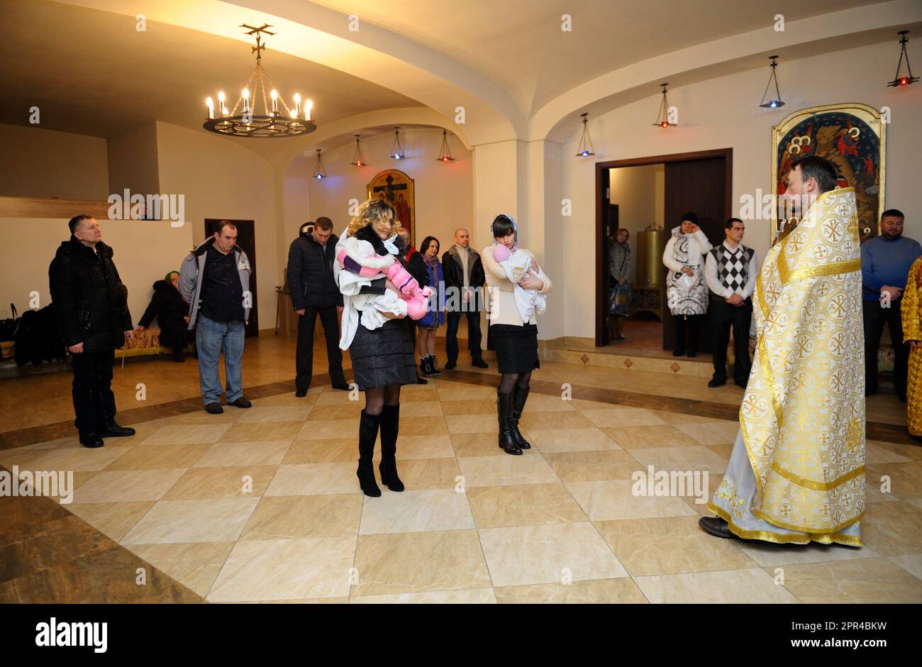 Priest standing in rural church in front of women holding abies on ...