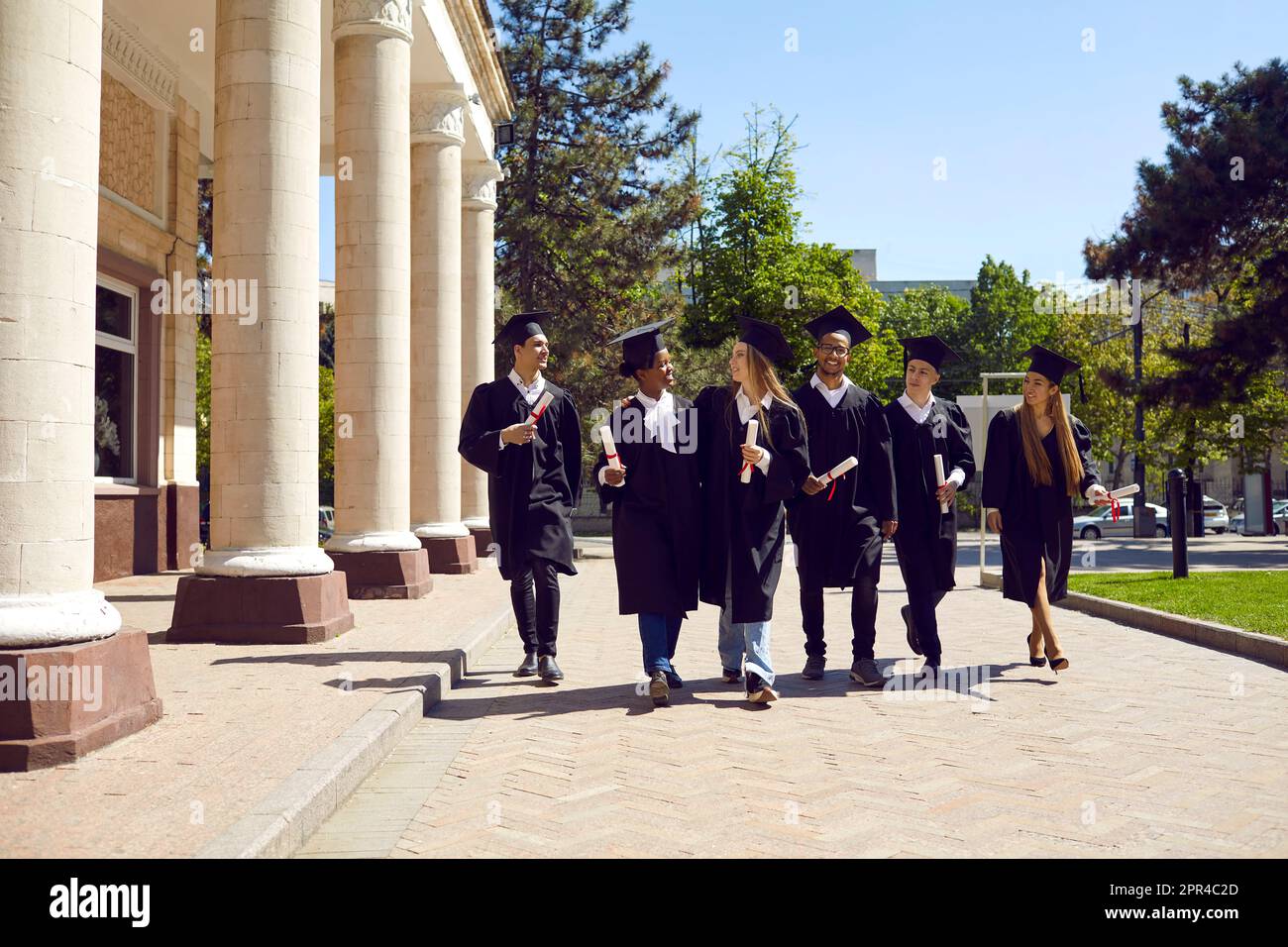 Group of happy diverse graduate students in caps and gowns walking ...