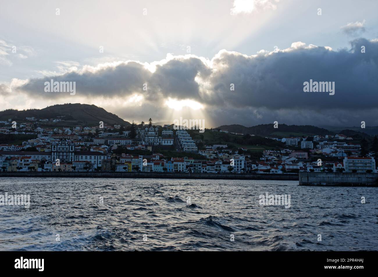 The sun sets behind the clouds over the town of Madalena, Pico island ...