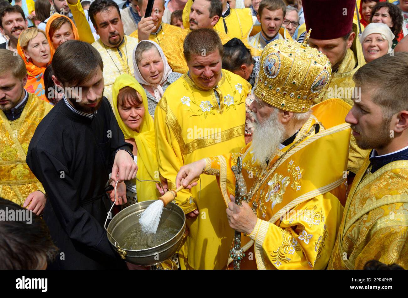 Orthodox priest blessing crowd of people with holy water. Ukrainian Orthodox Church of Kyiv ...
