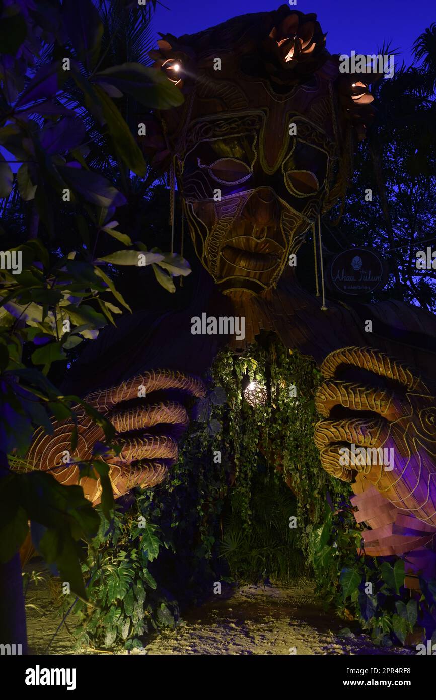 The Ahau Tulum Statue covered in lush green plants illuminated at night ...
