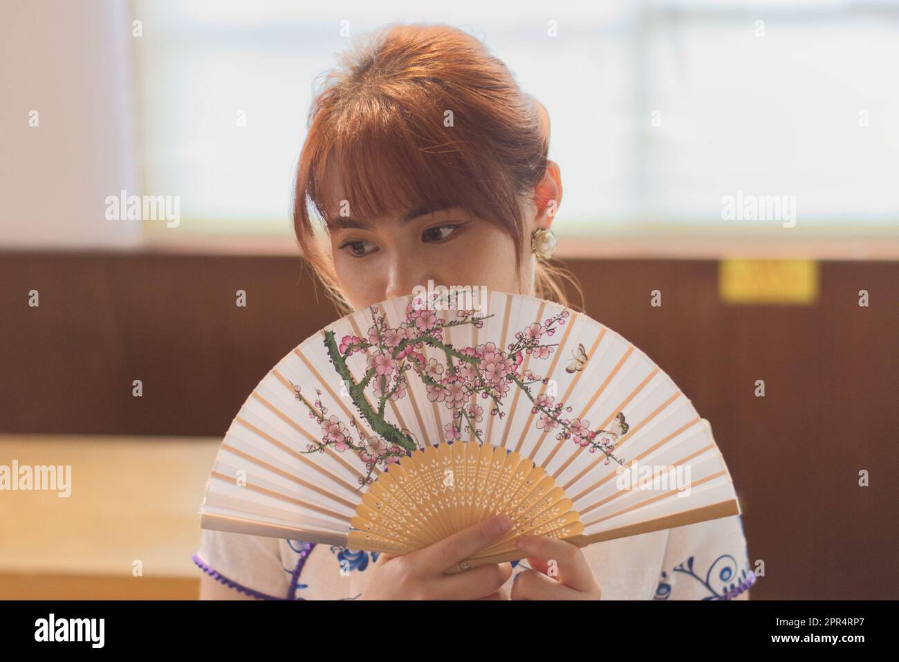 A young East Asian woman posing with an ornate oriental-style fan in ...