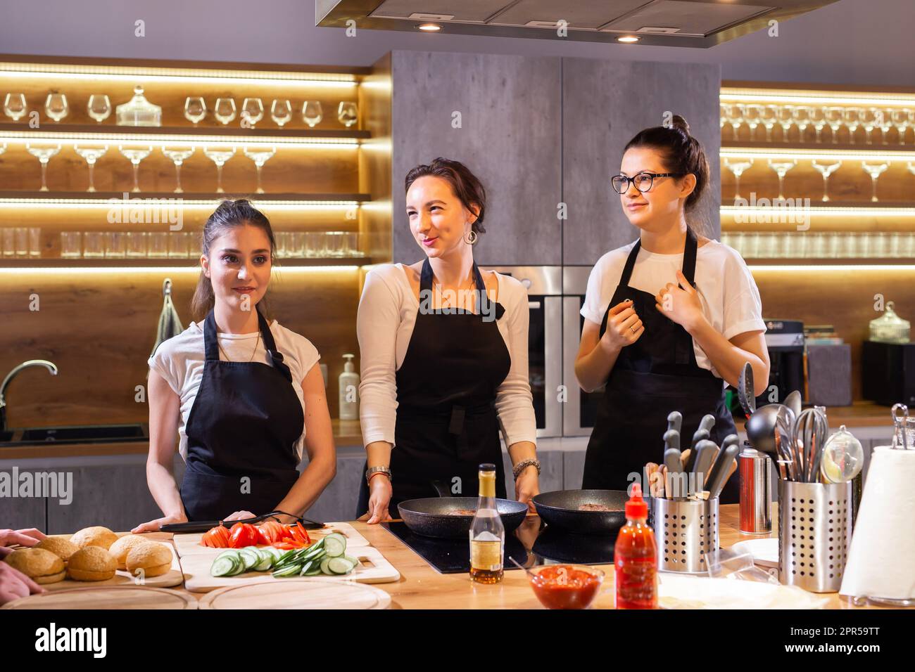 Three funny professional female chefs preparing food in large kitchen ...