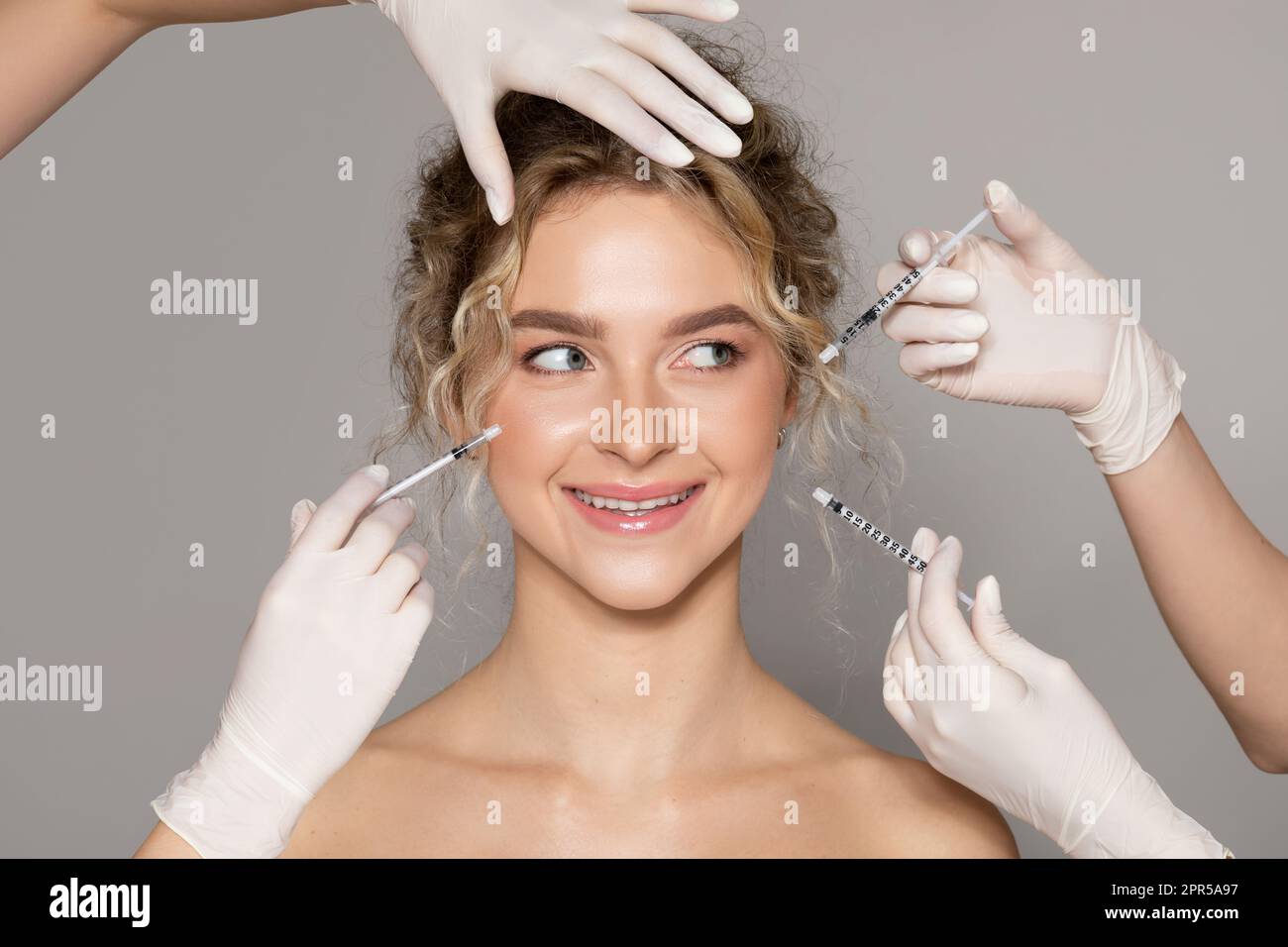 Beautiful lady getting facial injections by two cosmetologists, grey ...