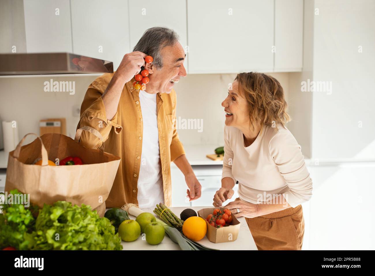 Joyful senior spouses taking out vegetables from paper bag after ...