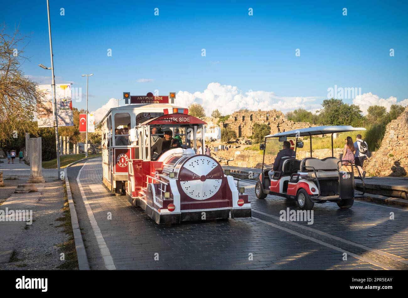 An electric buggy passes tourists travelling on a fake train or tram ...