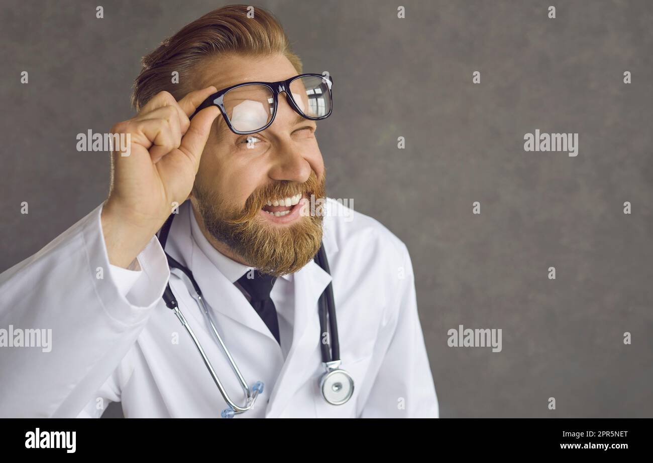 Funny happy doctor takes off glasses, winks eye and smiles on grey copy ...