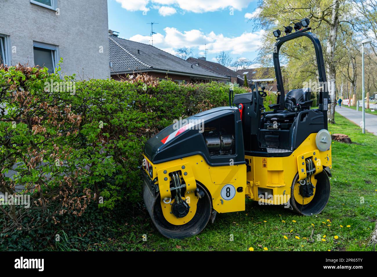 A small road-building roller of yellow-black color standing on the lawn ...
