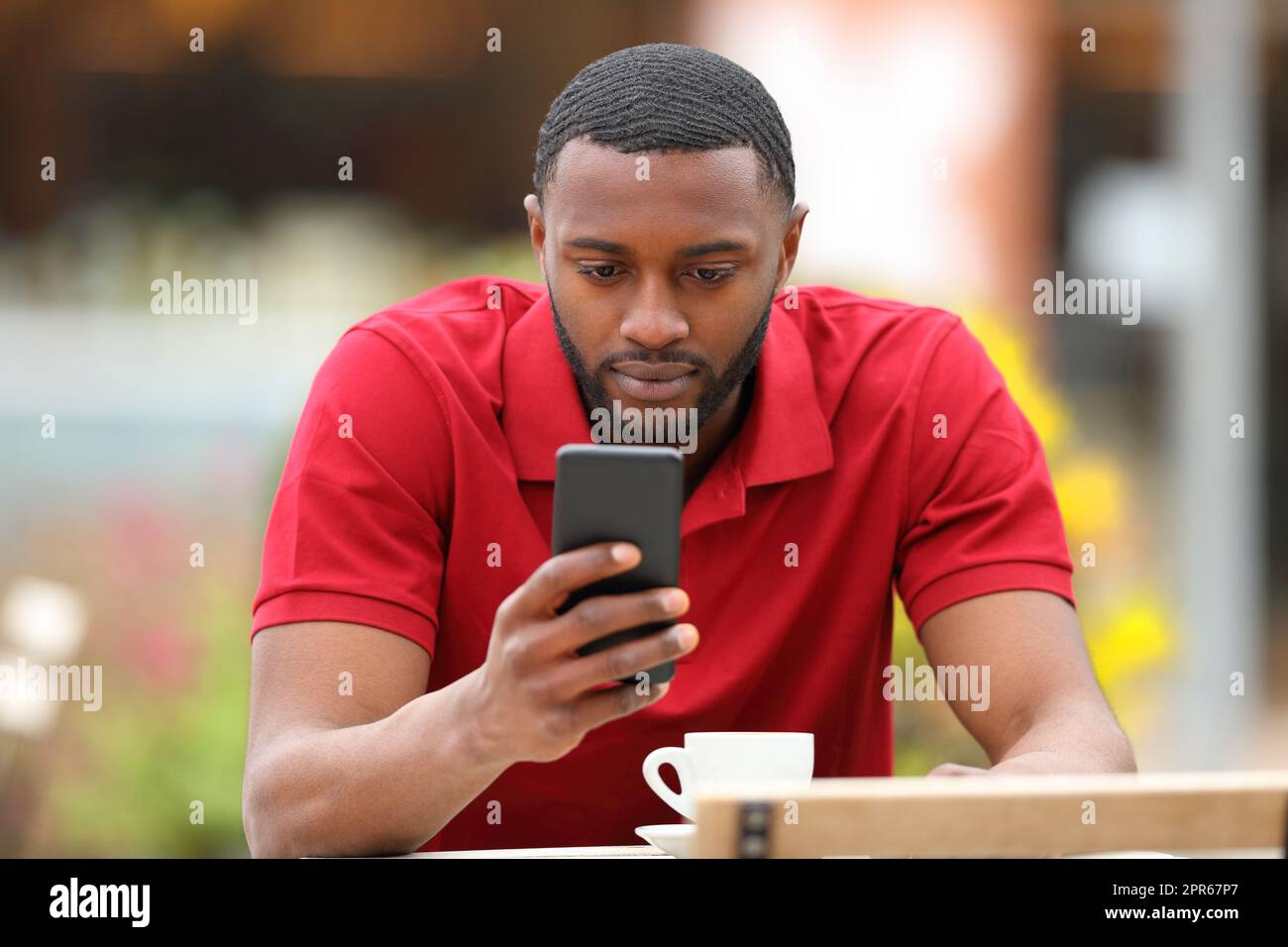Serious black man using cell phone in a bar terrace Stock Photo - Alamy