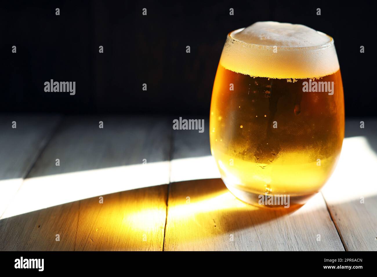 A frothy beer poured into a short, rounded glass illuminated by the ...