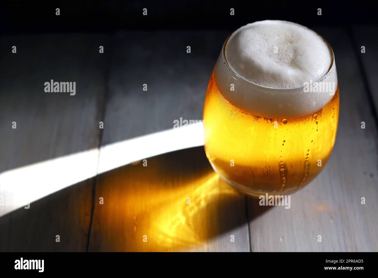 A frothy beer poured into a short, rounded glass illuminated by the ...