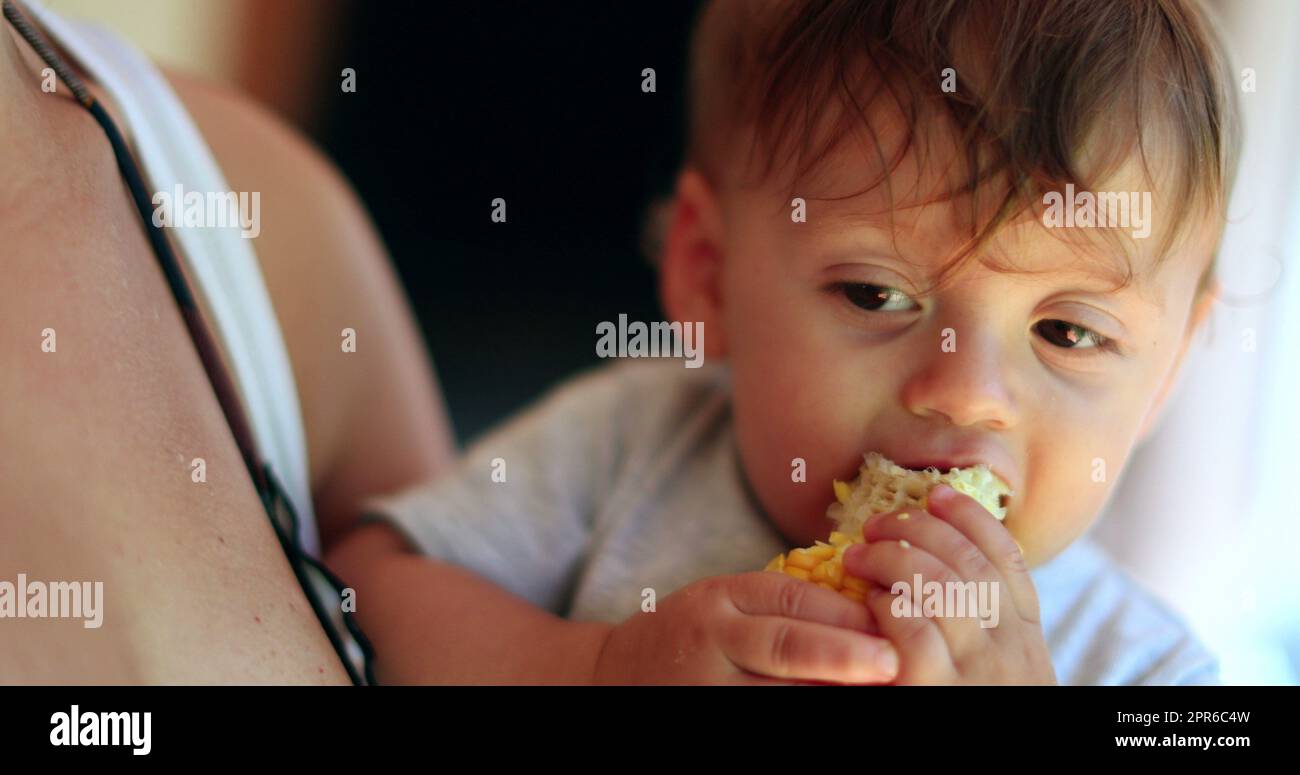 Happy baby eating corn. One year old toddler eats healthy natural snack ...
