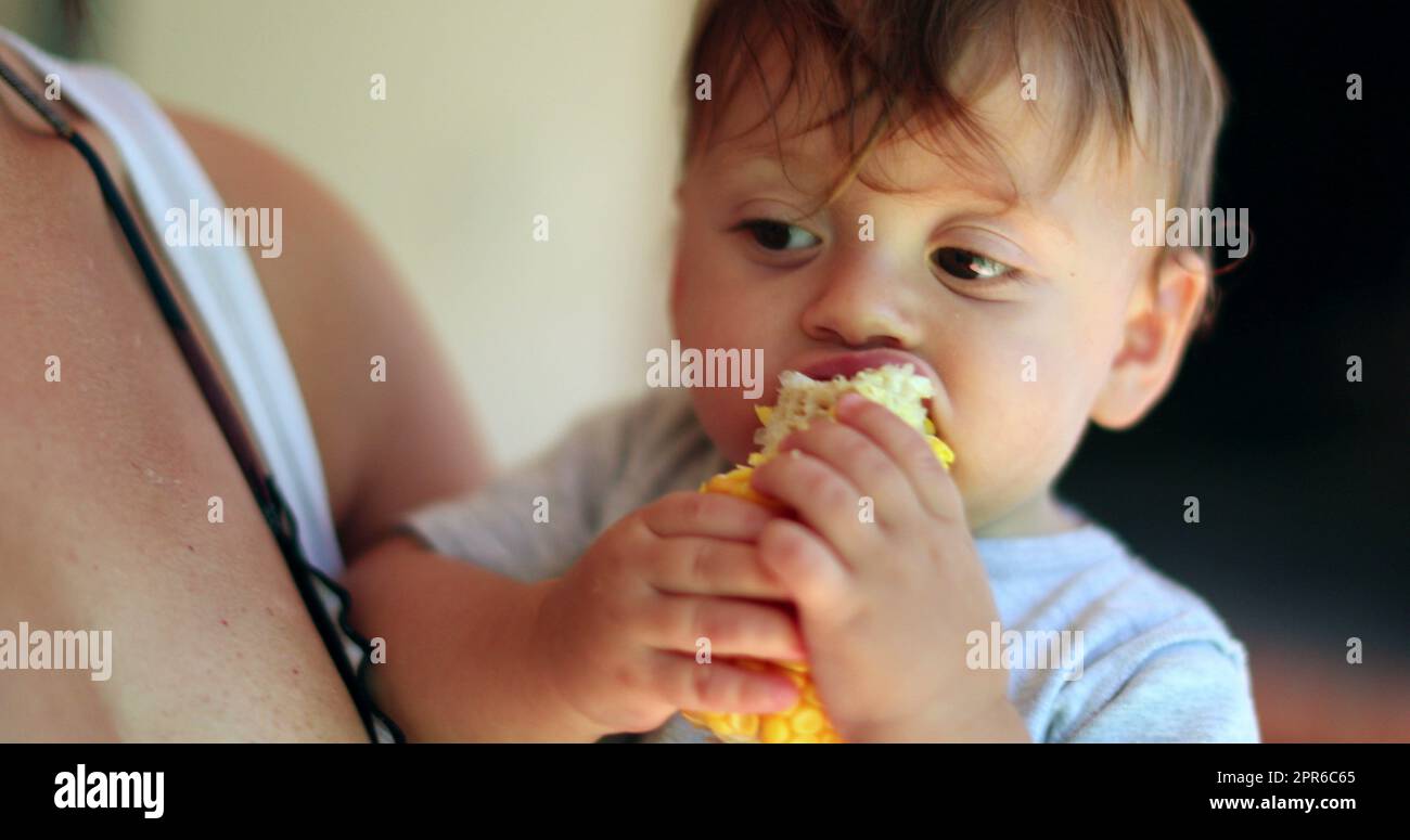Happy baby eating corn. One year old toddler eats healthy natural snack ...