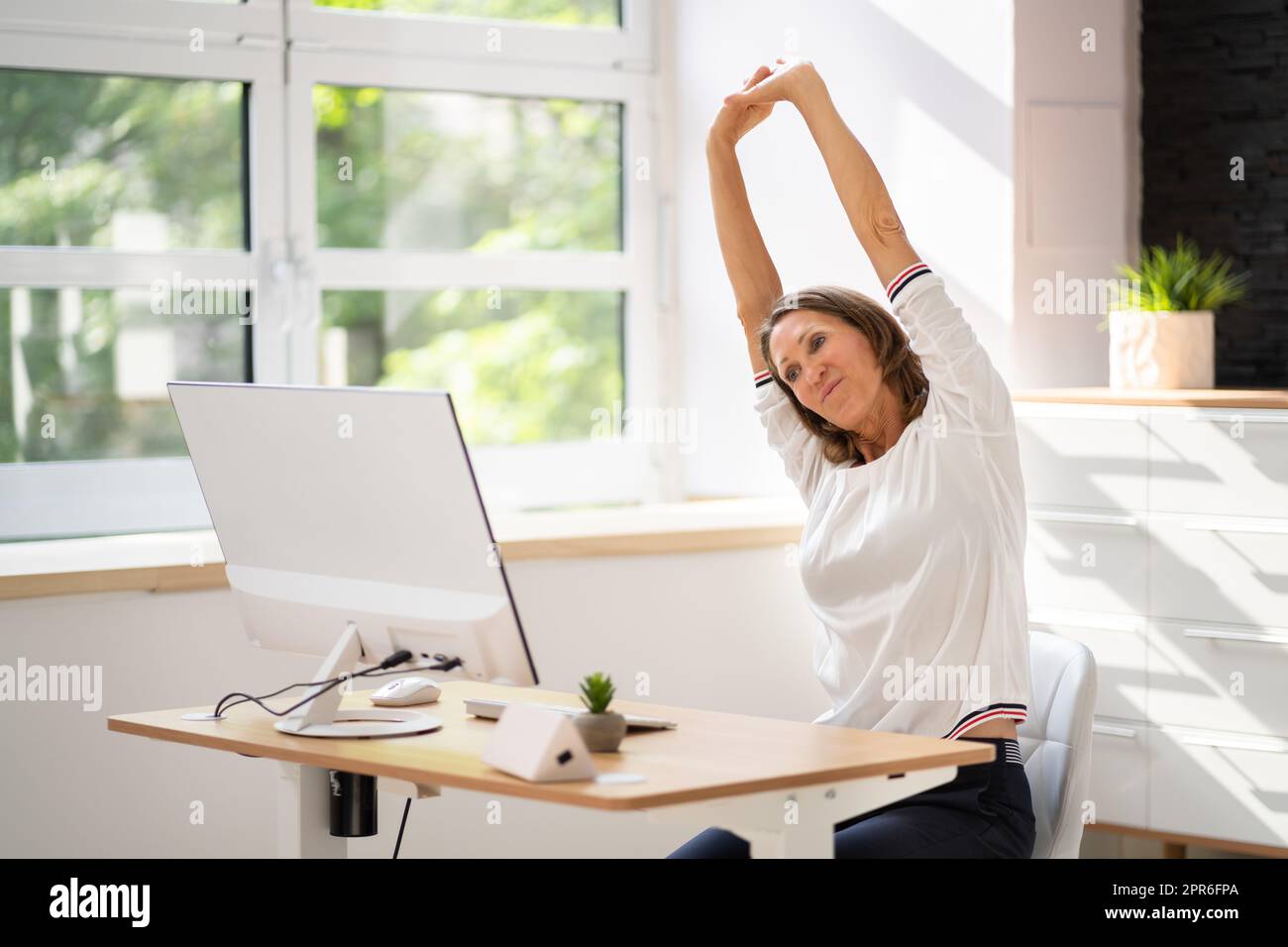 Woman Stretches At Office Desk Stock Photo - Alamy