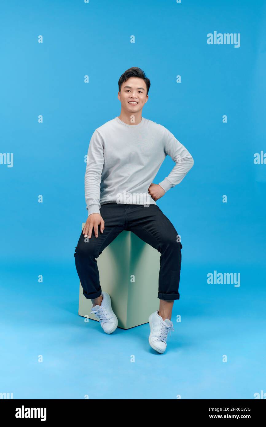 Full length photo of handsome man sitting cube over blue background ...