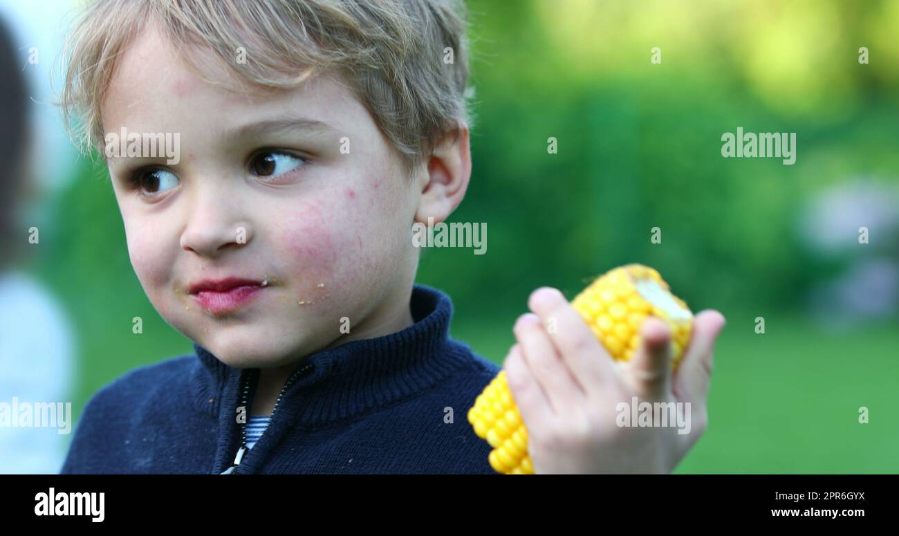 Happy infant toddler eating corn outside. Funny baby boy holding and ...