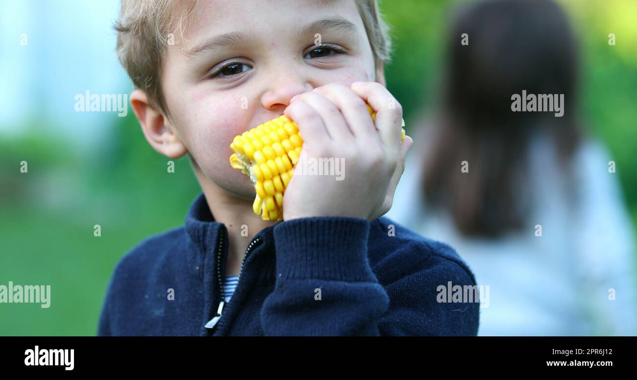 Happy infant toddler eating corn outside. Funny baby boy holding and ...