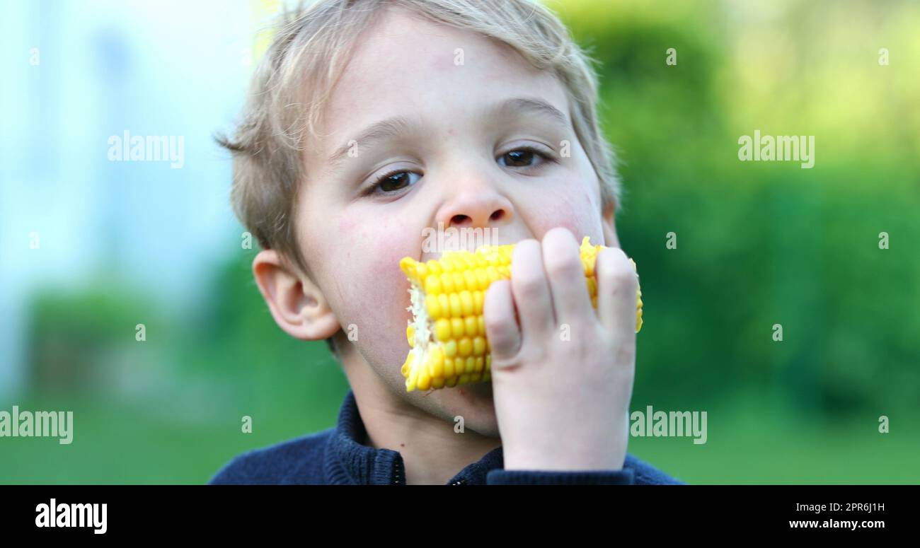 Happy infant toddler eating corn outside. Funny baby boy holding and ...