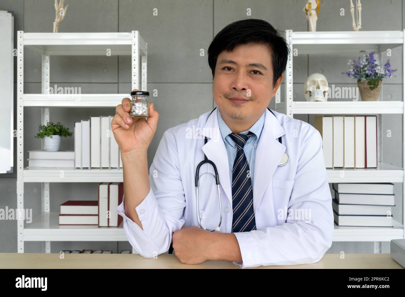 Asian doctor in white gown and stethoscope holding medical capsule ...