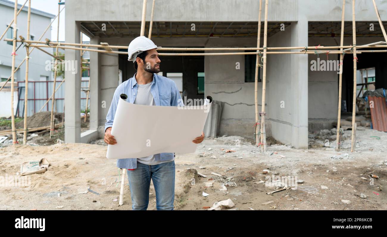 Young engineer in a construction helmet holding a floor plan while ...
