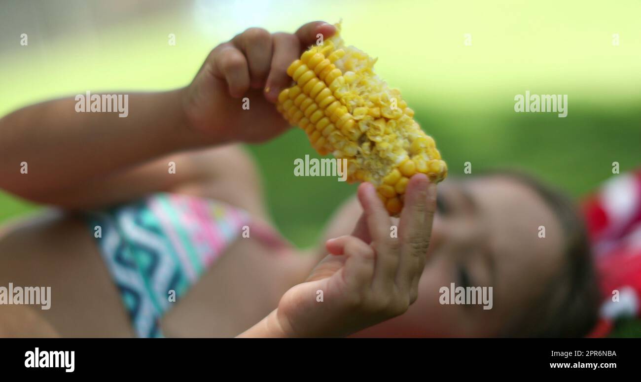 Little girl eating corn outside laid in grass. Child daydreaming while ...