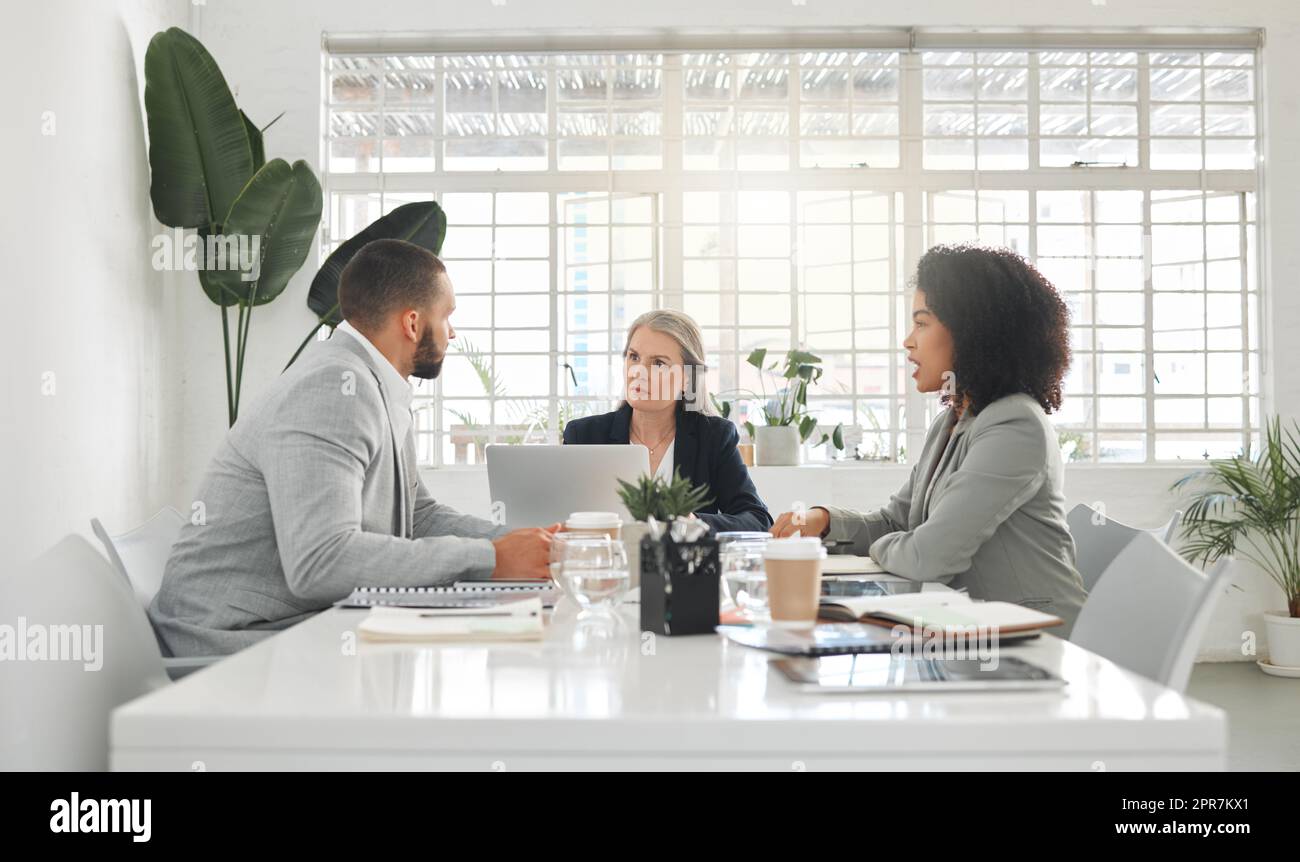 Three businesspeople having a meeting together at a table at work ...