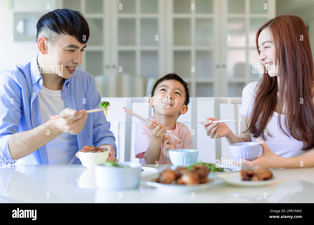 little boy enjoy eating food with father and mother. Happy Asian family having dinner at home ...