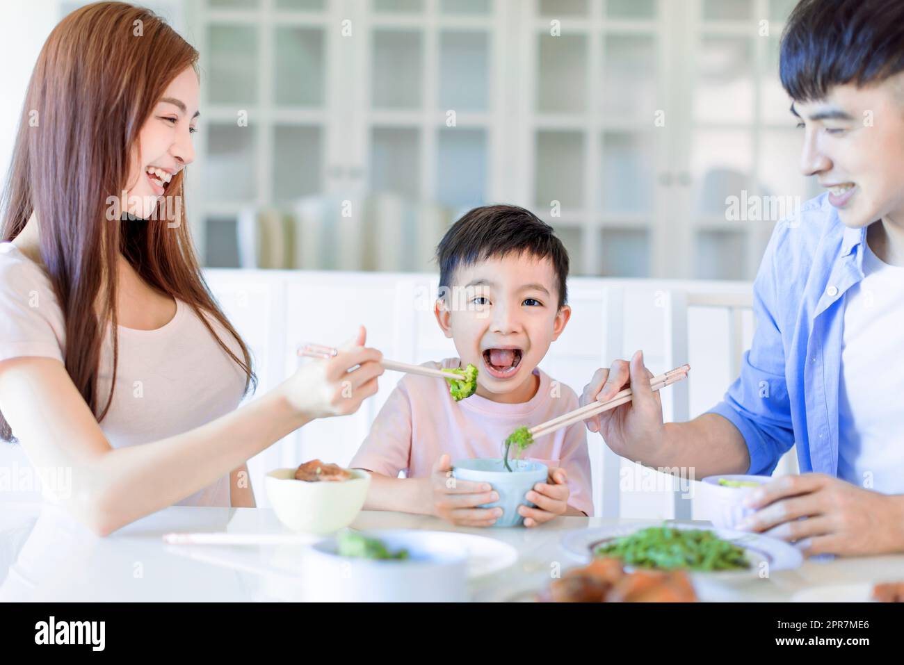 little boy enjoy eating food with father and mother. Happy Asian family having dinner at home ...