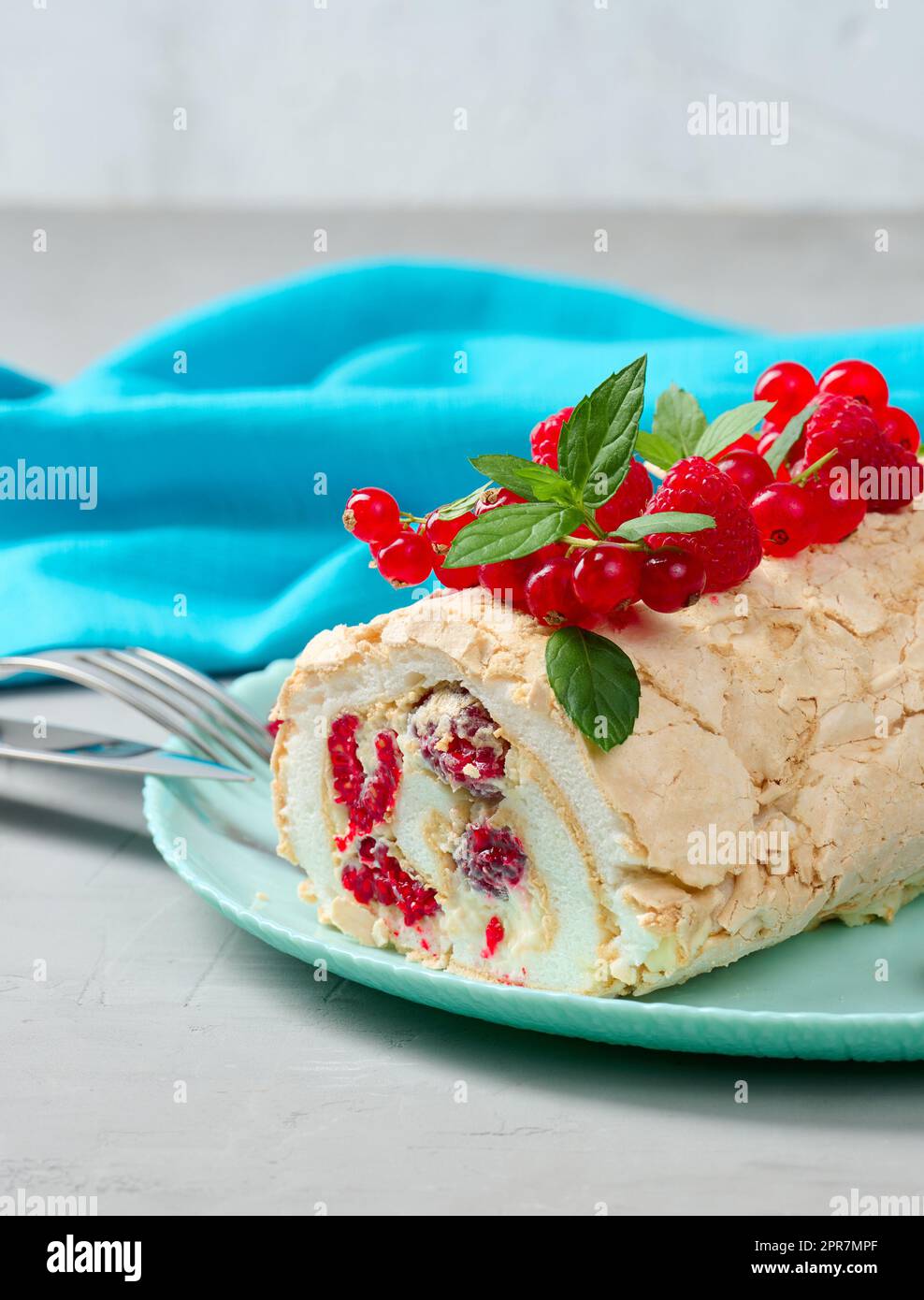 Baked meringue roll with red berries on a round plate, white background ...
