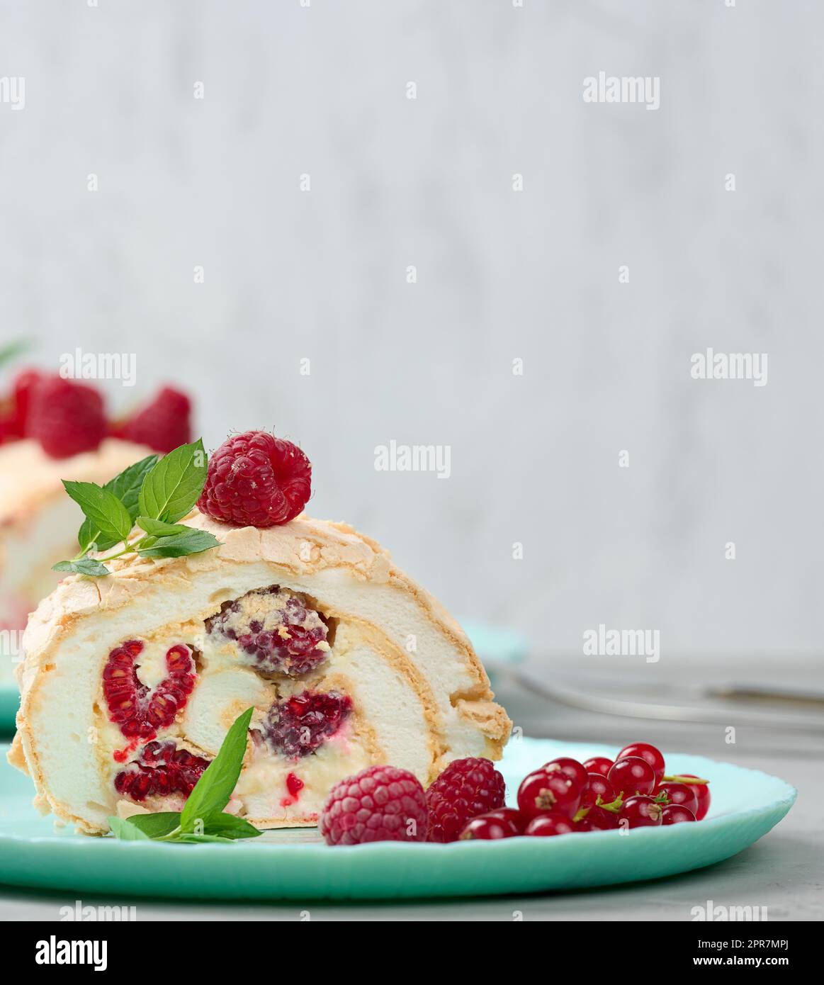 Baked meringue roll with red berries on a round plate, white background ...