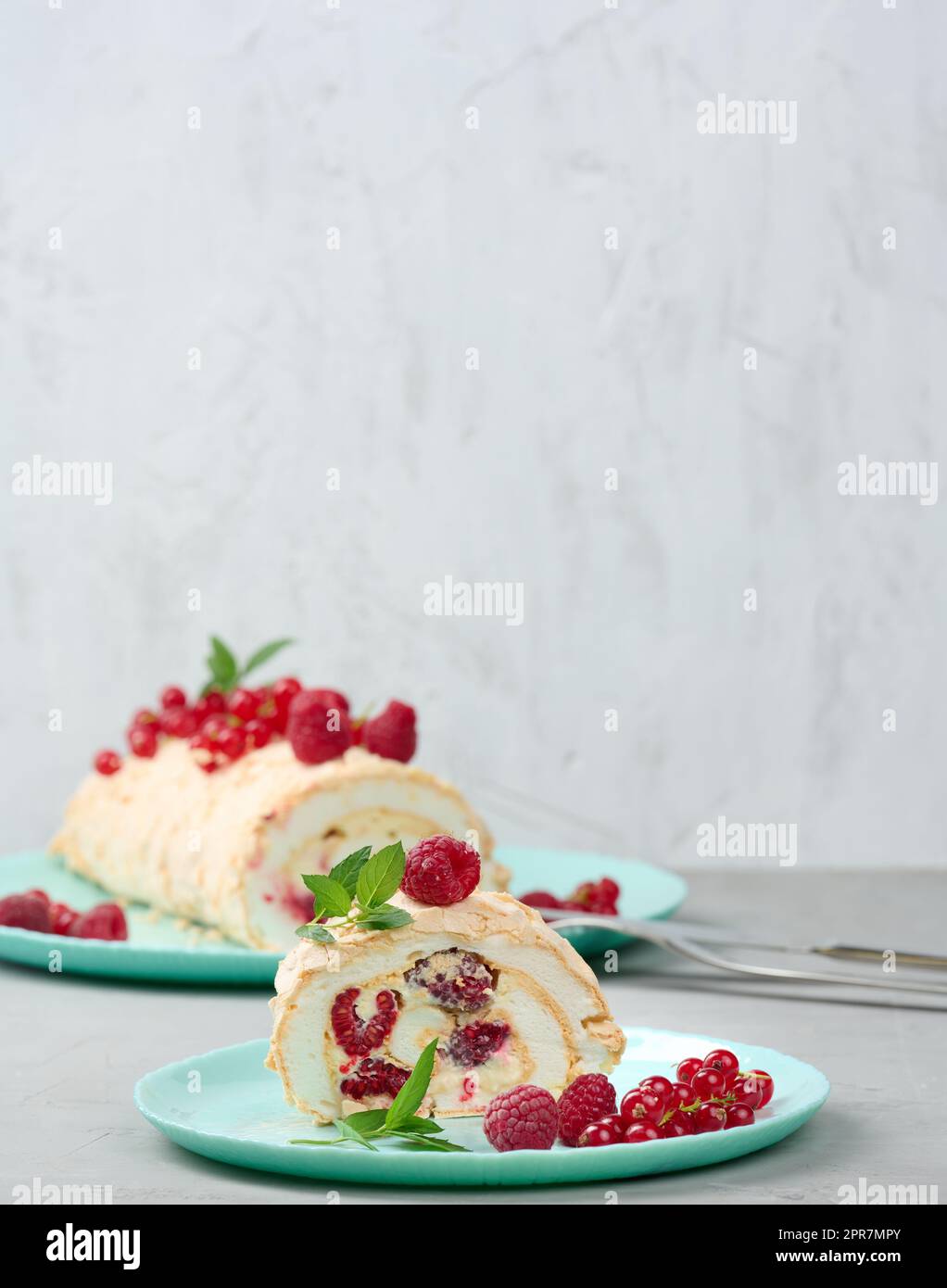 Baked meringue roll with red berries on a round plate, white background ...