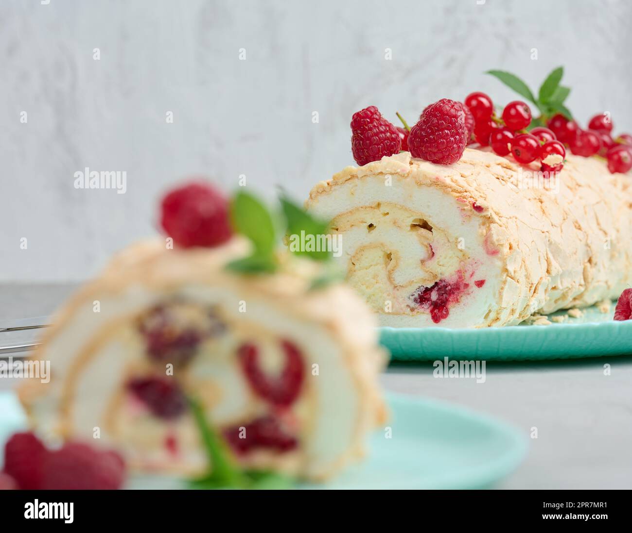 Baked meringue roll with red berries on a round plate, white background ...