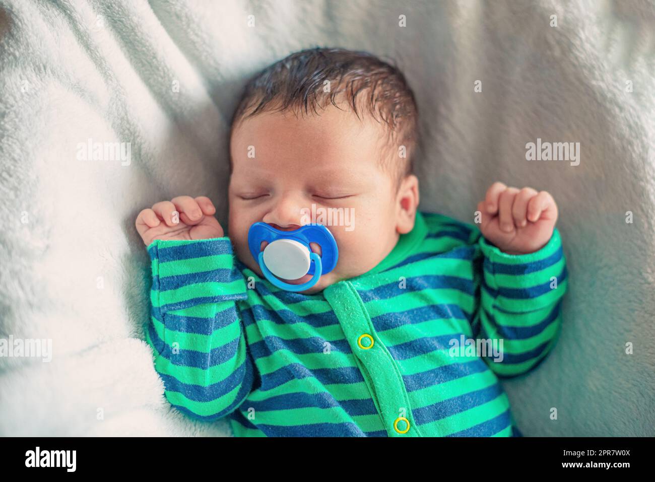 Sleeping newborn baby with raised arms and a pacifier in his mouth ...