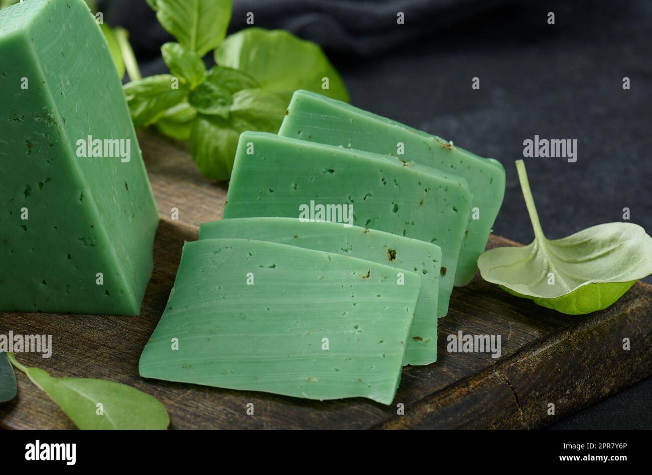 A piece of green cheese with basil on a brown wooden board, black ...
