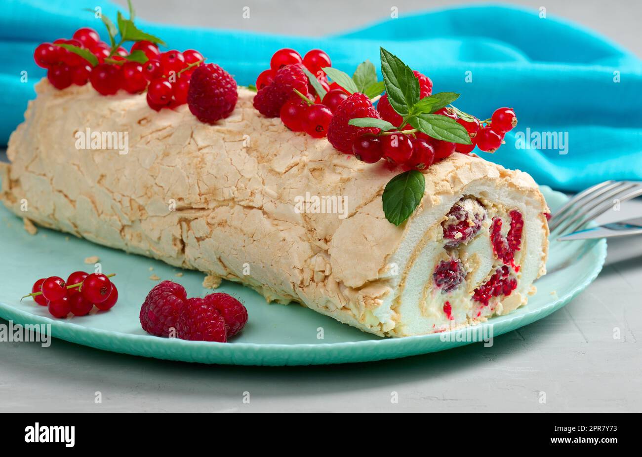 Baked meringue roll with red berries on a round plate, white background ...