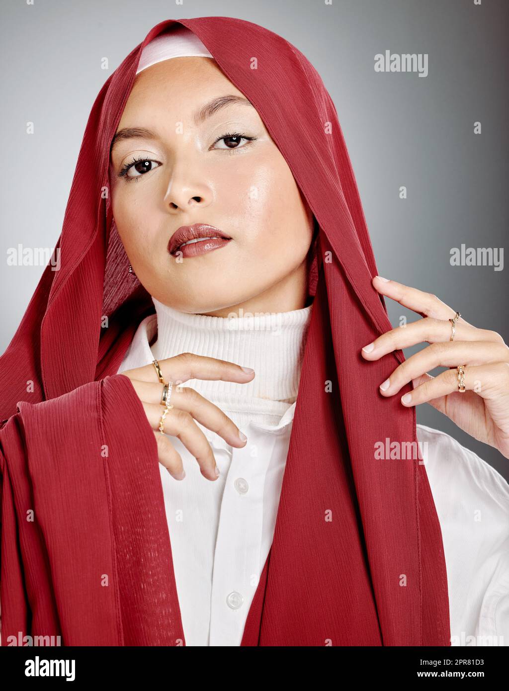 Portrait of a woman wearing a red hijab against grey studio background ...