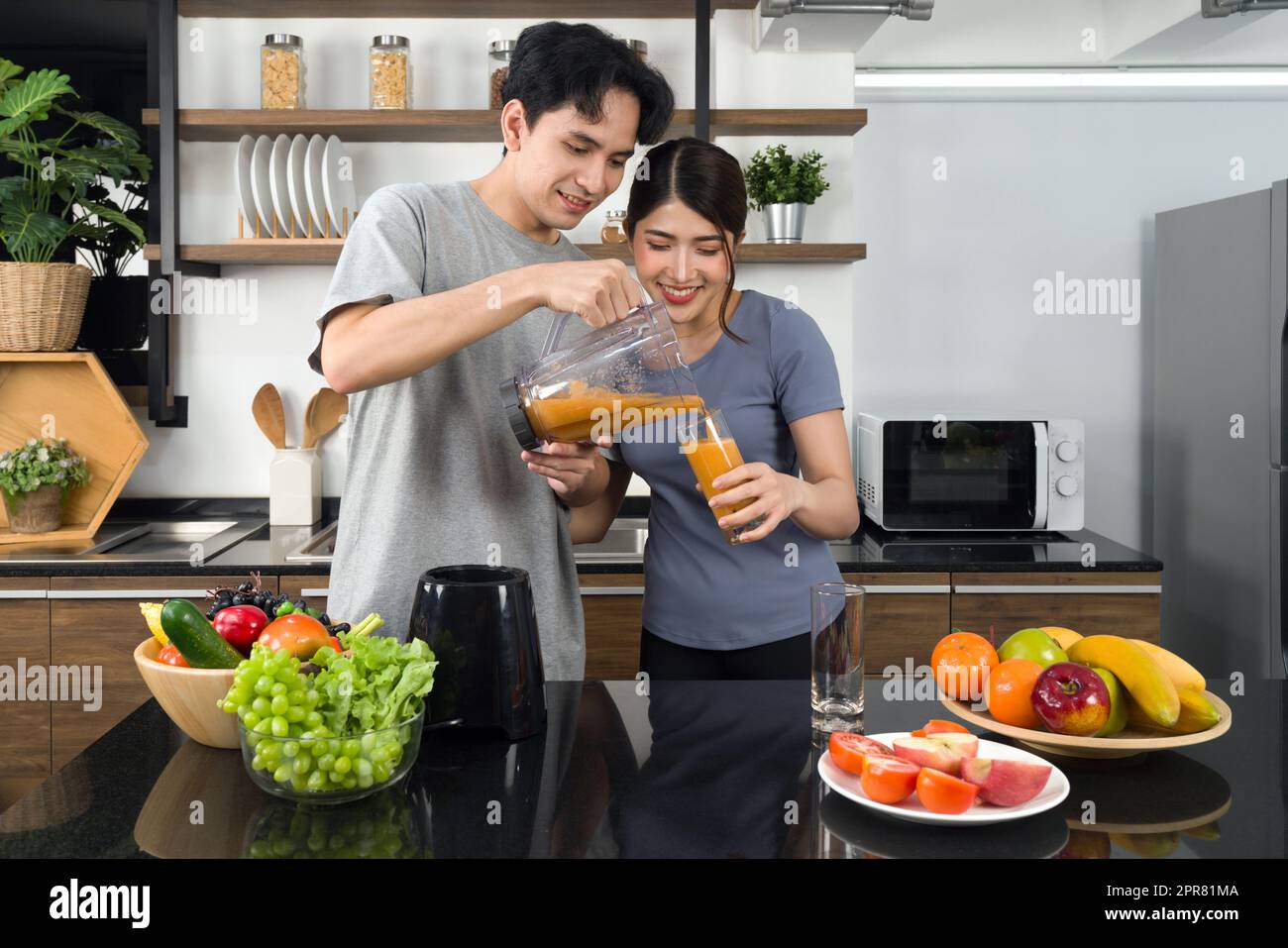 Young man in casual clothe pour mixed fruit and veggie smoothie from blending machine into his ...