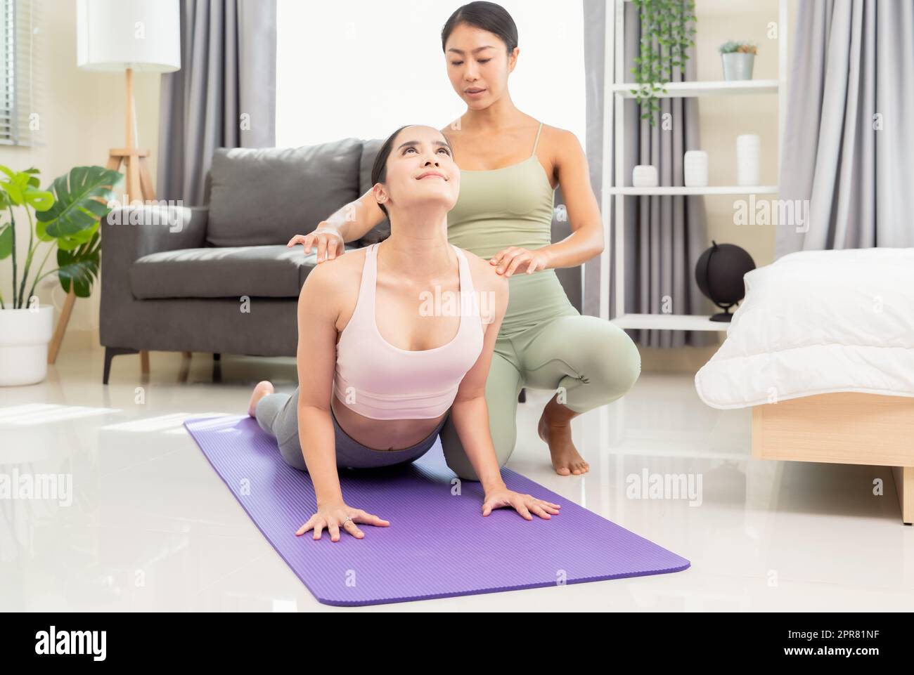 Two beautiful sporty girls practice yoga with partner at home. Trainer ...