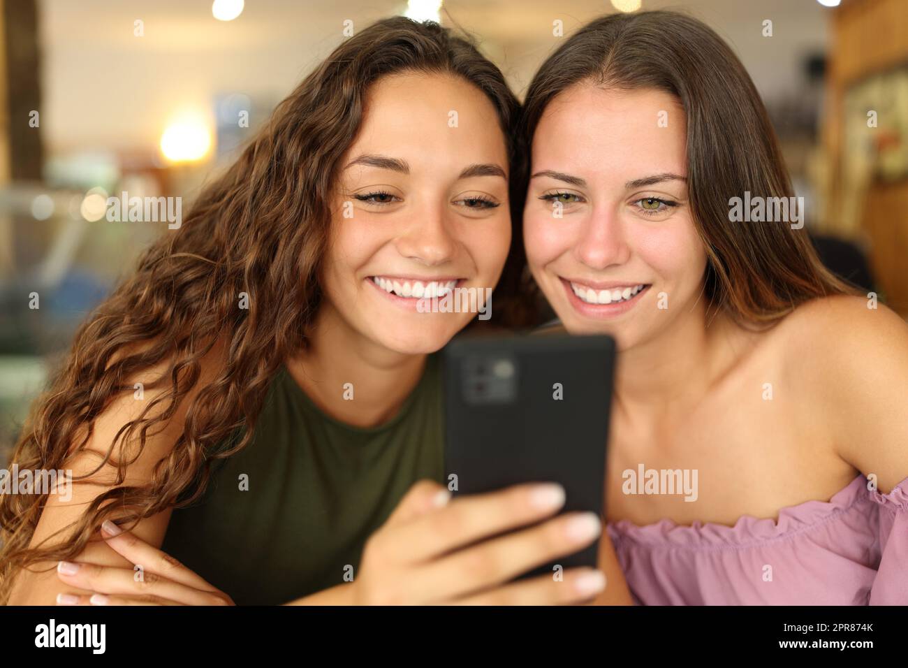 Women smiling checking smart phone together in a bar Stock Photo - Alamy