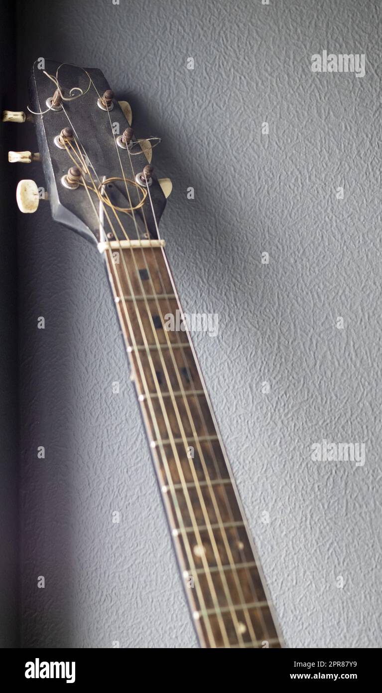 An acoustic old guitar in dust stands against a gray wall with copy ...