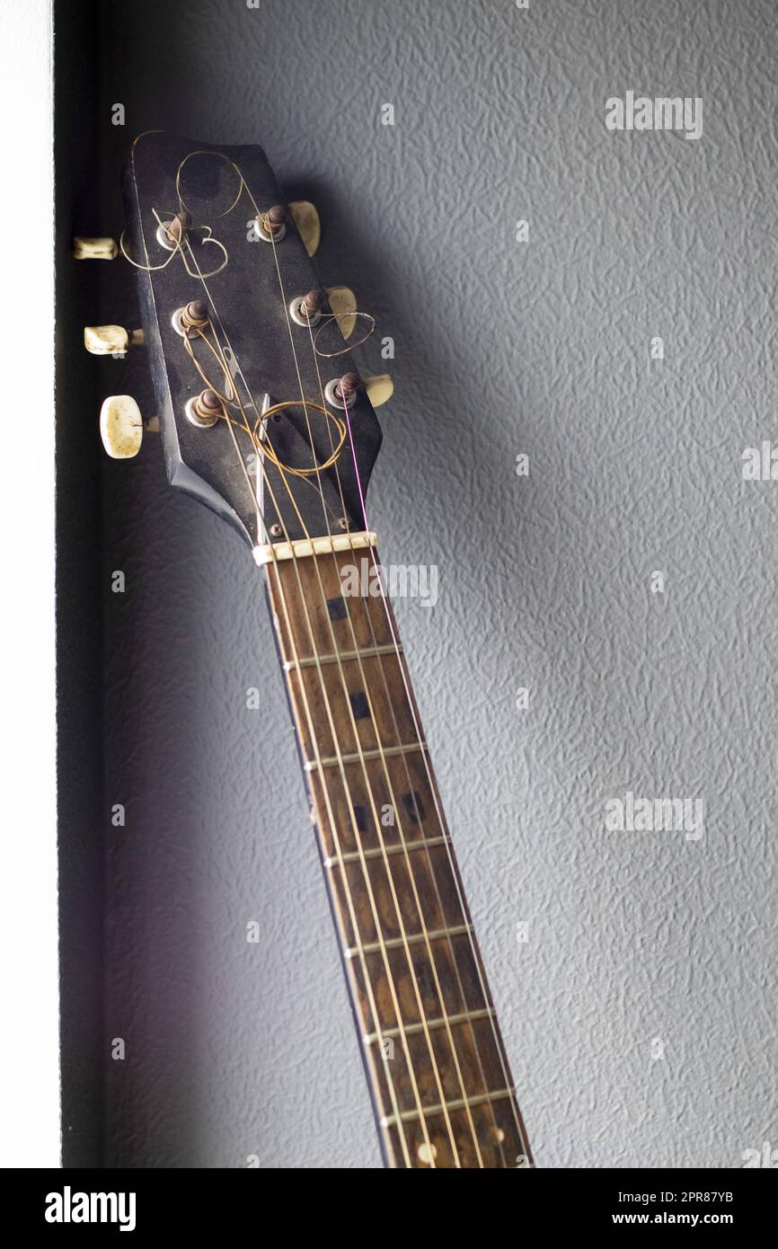 An acoustic old guitar in dust stands against a gray wall with copy ...