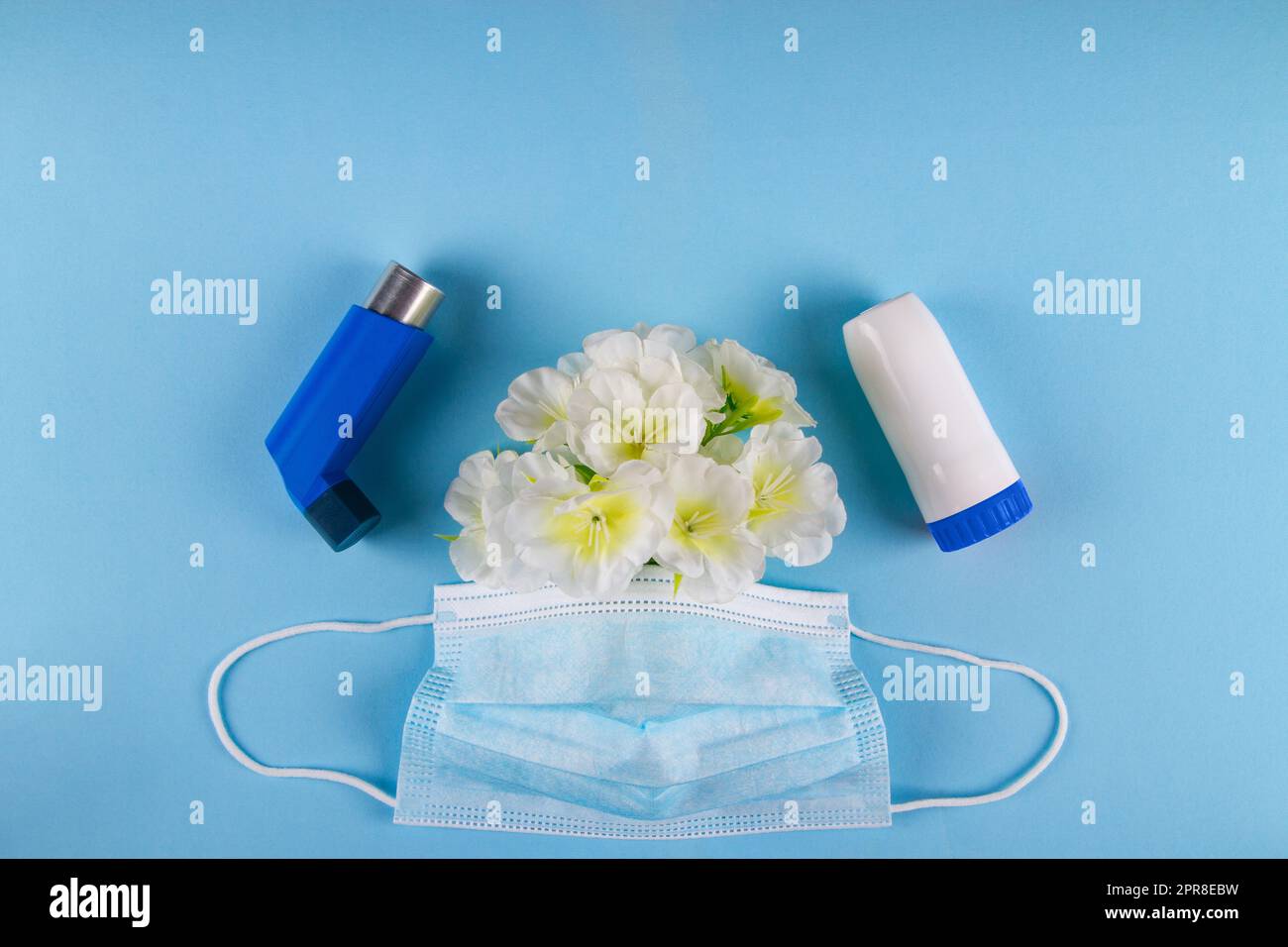 Two blue Inhalers, medical mask and white flowers on blue background ...