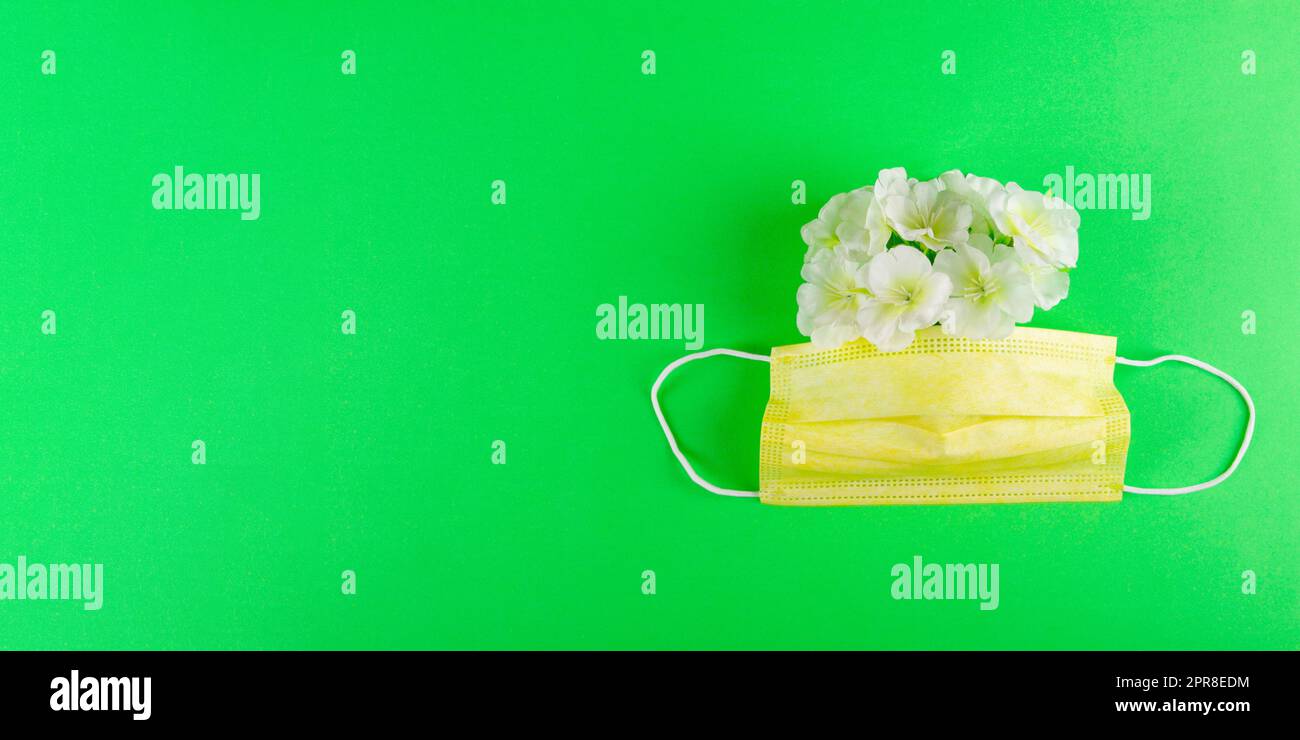 Yellow medical mask and white flowers on vibrant green background with ...